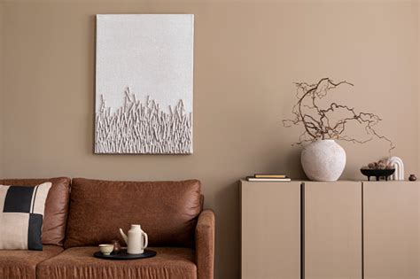 모형 포스터 프레임 갈색 소파 무늬 베개 베이지색 투수 가지가 있는 꽃병 개인 액세서리가 있는 아늑한 거실 인테리어의 미적 구성 가정 장식 템플렛 0명에 대한 스톡 사진 및