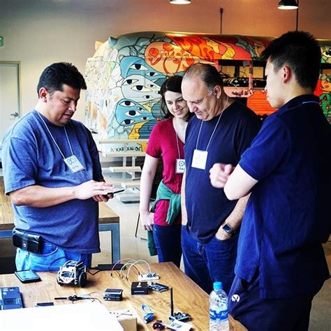 Four People Standing Around A Table With Electronics On It And One
