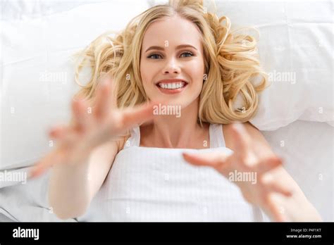 Top View Of Attractive Blonde Girl Smiling At Camera While Lying In Bed