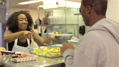 Volunteers In Kitchen Of Homeless Shelter Serves Food To People