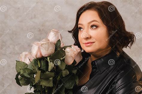 A Stylish Adult Woman In Black Leather Clothes Stands With A Bouquet Of