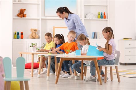 유치원의 책상에서 그림을 그리고 종이를 자르는 귀여운 어린 아이들의 그룹과 함께 보육 교사 놀이 시간 활동 20 24세에 대한 스톡 사진 및 기타 이미지 Istock