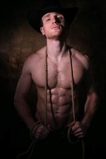 정의된 Pecs와 식스팩 복근 로프를 들고 있는 근육질의 팔을 보여주는 모자를 쓰고 있는 잘생긴 카우보이 남자에 대한 스톡 사진