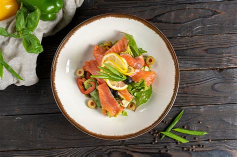 연어 또는 송어 샐러드 피망 올리브와 올리브 양파와 레몬으로 장식 나무 부엌 테이블에 세라믹 접시에 샐러드 잎과 붉은 물고기의 차가운 애피타이저 0명에 대한 스톡 사진 및