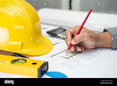 Asian Engineer With Plan Project Blueprint Graph And Yellow Helmet And