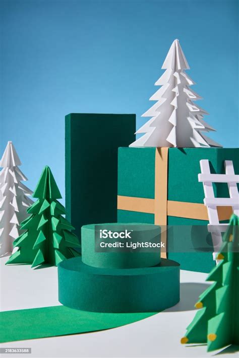 두 개의 둥근 연단이 서로 쌓여 녹색 종이 조각에 놓여 소나무 종이로 둘러싸여 있으며 파란색 배경에 흰색 사다리가 있는 녹색 선물 상자가 있습니다 사진 샘플에 대한