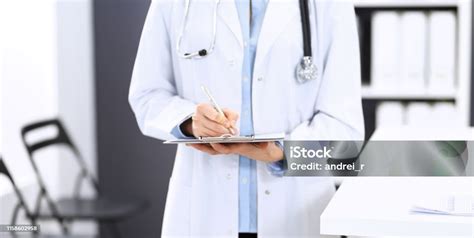 진료소 나 응급 병원의 리셉션 데스크 근처에 서있는 동안 의료 양식을 작성하는 의사 여성 직장에서 알 수없는 의사 손 클로즈업