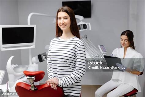 젊고 예쁜 소녀가 진료실의 치과 의자 옆에 서서 의사가 환자의 건강에 대해 메모하고 있습니다 2명에 대한 스톡 사진 및 기타 이미지 Istock