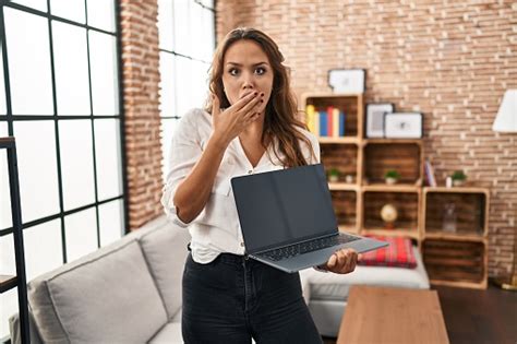 젊은 히스패닉 여성은 손으로 입을 가리는 집에서 빈 화면을 보여주는 노트북을 사용하여 충격을 받고 실수를 두려워합니다 놀란 표정 가리기에 대한 스톡 사진 및 기타 이미지