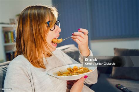 흰색 접시와 스웨터와 안경을 입고 숟가락을 들고 집에서 그녀의 침대 소파에 앉아 파스타 점심 이나 저녁 식사를 먹는 젊은 백인