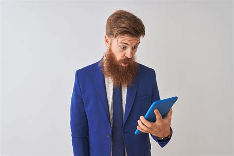젊은 빨간 머리 아일랜드어 사업가 를 사용하여 태블릿 위에 고립 된 흰색 배경 에 무서워 충격으로 충격 두려움과 두려움 표정흥분