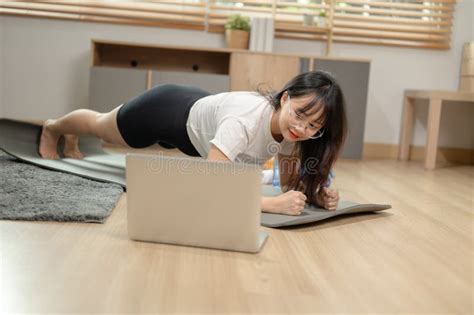A Strong Asian Woman Is Following An Online Workout Tutorial On Her