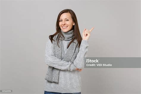 회색 스웨터 스카프 회색 벽 바탕에 옆으로 격리 하는 검지 손가락을 가리키는에서 매력적인 젊은 여자를 웃 고 건강 패션 라이프