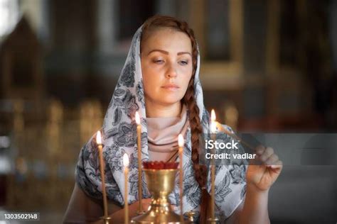붉은 머리와 머리에 스카프를 가진 러시아의 아름다운 백인 여성이 정교회에 있으며 촛불을 밝히고 아이콘 앞에서 기도합니다 교회에 대한 스톡 사진 및 기타 이미지 Istock