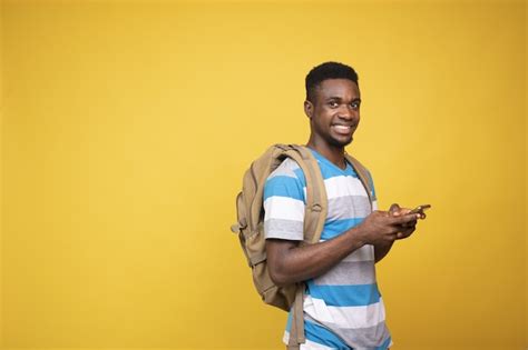 Jovem Do Sexo Masculino Com Uma Mochila Usando Seu Telefone Contra Um Fundo Amarelo Foto Gr Tis