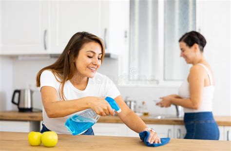 Woman Cleaning Countertop In Kitchen While Friend Washes Dishes Stock