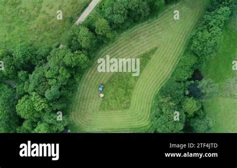 Top Down Aerial Of A Triangular Grass Field Being Cut In A Visually Pleasing Manner Blue
