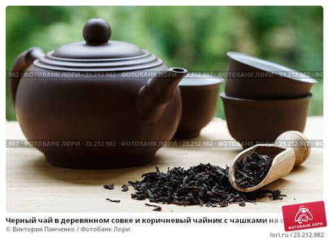 Черный чай в деревянном совке и коричневый чайник с чашками на столе ...