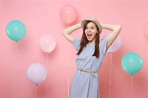 밀 짚 여름 모자와 화려한 공기 풍선 핑크 바탕에 머리 근처에 손을 유지 하는 파란 드레스를 입고 좋아 라 행복 한 젊은 여자의