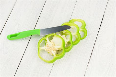 오래 된 시골 백색 나무 판자에 녹색 신선한 원료 고추와 녹색 플라스틱 손잡이 가진 금속 칼 슬라이스 0명에 대한 스톡 사진 및