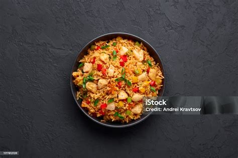 어두운 슬레이트 배경에 검은 그릇에 Schezwan 치킨 볶음밥 사천 쌀은 피망 녹색 콩 당근 닭 가슴살을 곁들인 인도 중국 요리 요리입니다 공간을 복사합니다 맨 위 보기