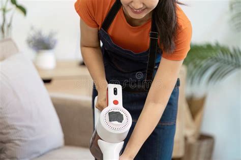 Young Woman Cleaning Living Room With Modern Vacuum Cleaner In Cozy