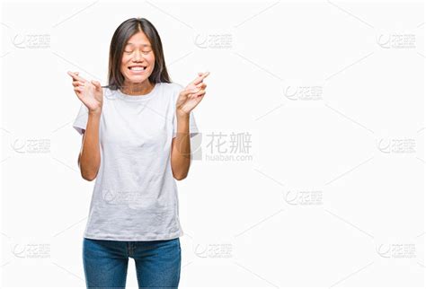 年轻的亚洲女子在孤立的背景微笑交叉手指，希望和眼睛闭上。运气和迷信的概念。