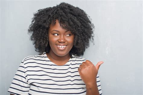 젊은 아프리카계 미국인 플러스 크기 여자 생기고 엄지 측면 가리키는 행복 한 얼굴로 웃 고 회색 그런 지 벽에 T 셔츠에 대한