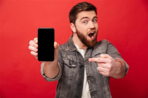 스마트 폰에 손가락을 가리키는 즐거운 성인 남자의 이미지와 카메라에 흥분을 표현 빨간색 배경에 고립 가리키기에 대한 스톡 사진