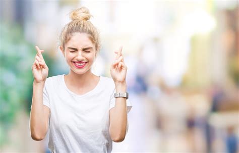 젊은 아름 다운 금발 여자를 입고 흰색 티셔츠는 고립 된 배경으로 희망과 눈이 닫힌 손가락으로 건너 웃 고 있습니다 행운과 미신 개념입니다 금발 머리에 대한 스톡 사진 및