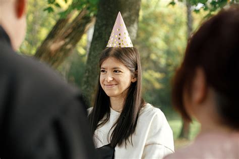 야외 에서 피크닉 파티에서 가족 및 친구들과 생일을 축하하는 파티 모자를 쓴 세련된 젊은 여성 어머니와 아버지는 생일에 딸을 축하합니다 공원에서 가족 모임 사람들에 대한