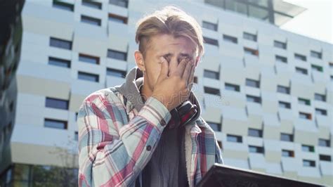 Молодой парень в очках сидит на улице с ноутбуком Он принимает свои