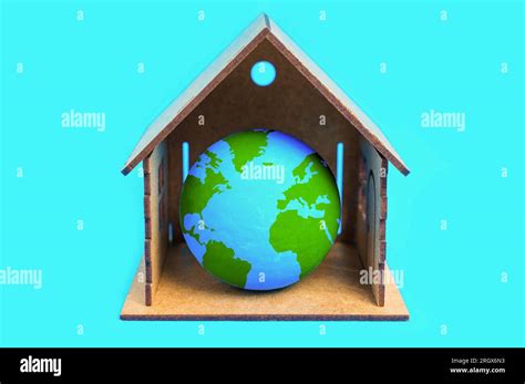 Tiny Globe Model Nestled Within A Miniature Wooden House Isolated On Blue Sustainable Living