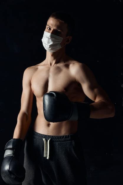 Boxeador culturista en una máscara médica sobre un fondo negro guantes atleta torso desnudo