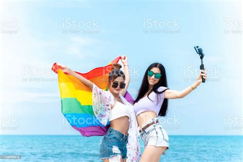 해변에서 Lgbtq 깃발을 가진 레즈비언 커플 바다에서 함께 휴가를 보내는 행복한 커플 2명에 대한 스톡 사진 및 기타 이미지