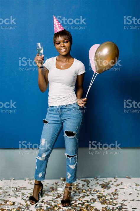 파란색 배경 위에 고립 된 풍선과 샴페인무리를 들고있는 쾌활한 젊은 아프리카 여성의 전체 길이 초상화 생일 파티 축 하 컨셉 감정에 대한 스톡 사진 및 기타 이미지 Istock