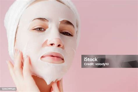 아름다운 젊은 여자는 분홍색 배경에 얼굴에 화장품 티슈 마스크를 적용 페이셜 마스크에 대한 스톡 사진 및 기타 이미지 페이셜 마스크 직물 여자 Istock