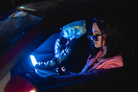 미래형 안경을 쓰고 차 안에서 휴대전화를 사용하는 두 여성의 여성 초상화 필름 누아르 스타일과 사이버 펑크 컨셉 사진 네온 불빛이있는 영화 사진 파란 헤어스타일 차량에 있는
