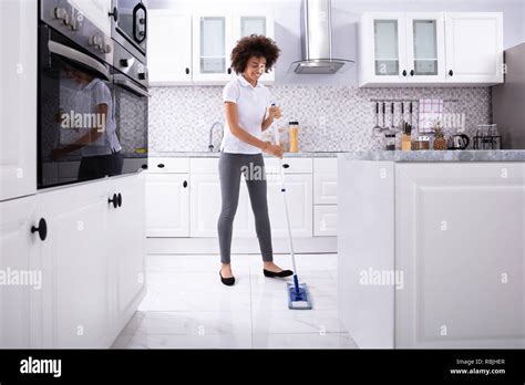 Side View Of A Smiling Female Janitor Cleaning White Floor With Mop In