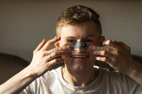 Smiling Young Man Applying Black Nose Patch To Clean Pore Skin And