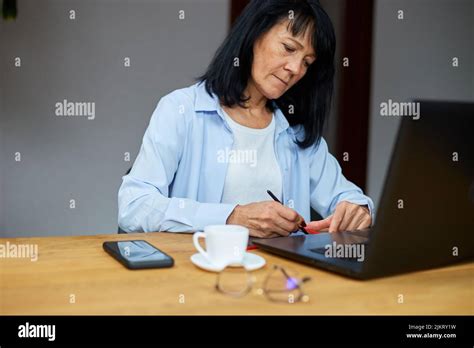Mature Woman Designer Drawing With Graphics Tablet And Stylus Working At Laptop Using Computer