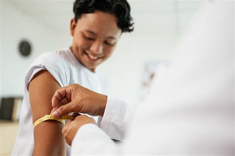 일반 개업의 또는 영양사를 방문하는 십대 소년 소년의 팔과 허리를 측정하는 의사와 함께 아시아 가족 12 13세에 대한 스톡
