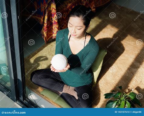 Pretty Chinese Young Woman Meditating At Home Sitting On Floor Holding