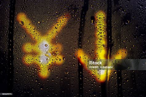 전구로 만든 아래쪽 화살표가 있는 흐릿하게 빛나는 일본 엔 기호 밤에는 물방울이 떨어지는 비에 젖은 창문 뒤에 있는 국가 통화의 상징 경제 위기의 징후 감가상각에 대한 스톡