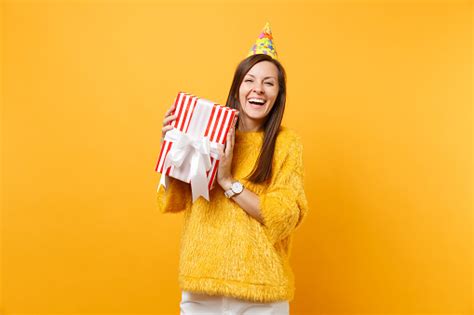 밝은 노란색 배경에 고립 된 휴가 즐기는 생일 파티 모자 들고 빨간색 상자 선물 축 하는 존재 여자를 웃 고 있다 사람들이