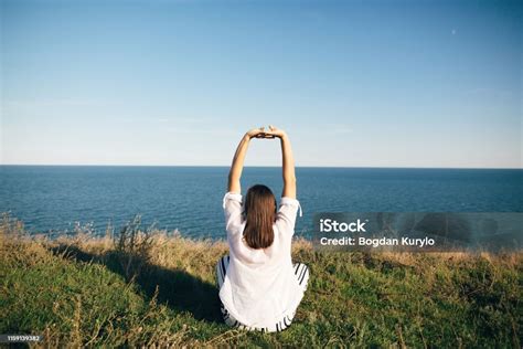 바다와 하늘을 볼 수있는 산 봉우리에 앉아 요가를하는 세련된 힙스터 소녀 요가와 명상을 연습 행복한 여자 텍스트의 공백입니다
