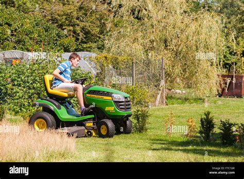 A 15 year old boy mowing the lawn on a John Deere ride on mower in the ...