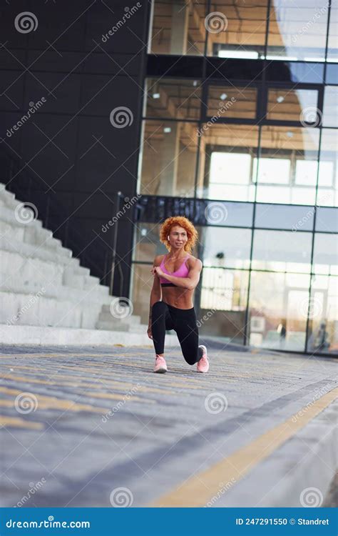 Young European Redhead Woman In Sportive Clothes Doing Squats Outdoors