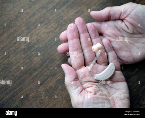 Two Aged Hands Hold A Hearing Device Copy Space Concept Of The