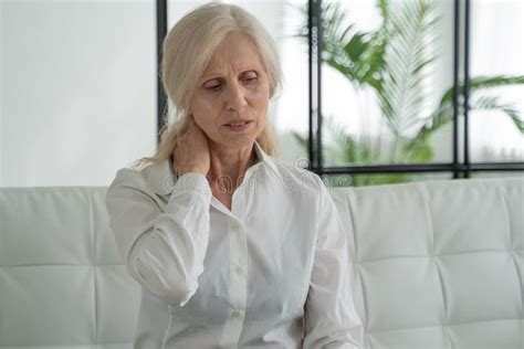 Elderly Woman Suffering From Neck Pain Sitting On The Couch At Home